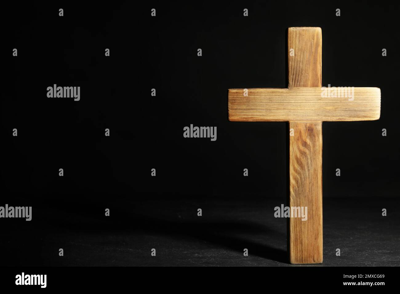 Wooden Christian cross on black slate table against dark background ...