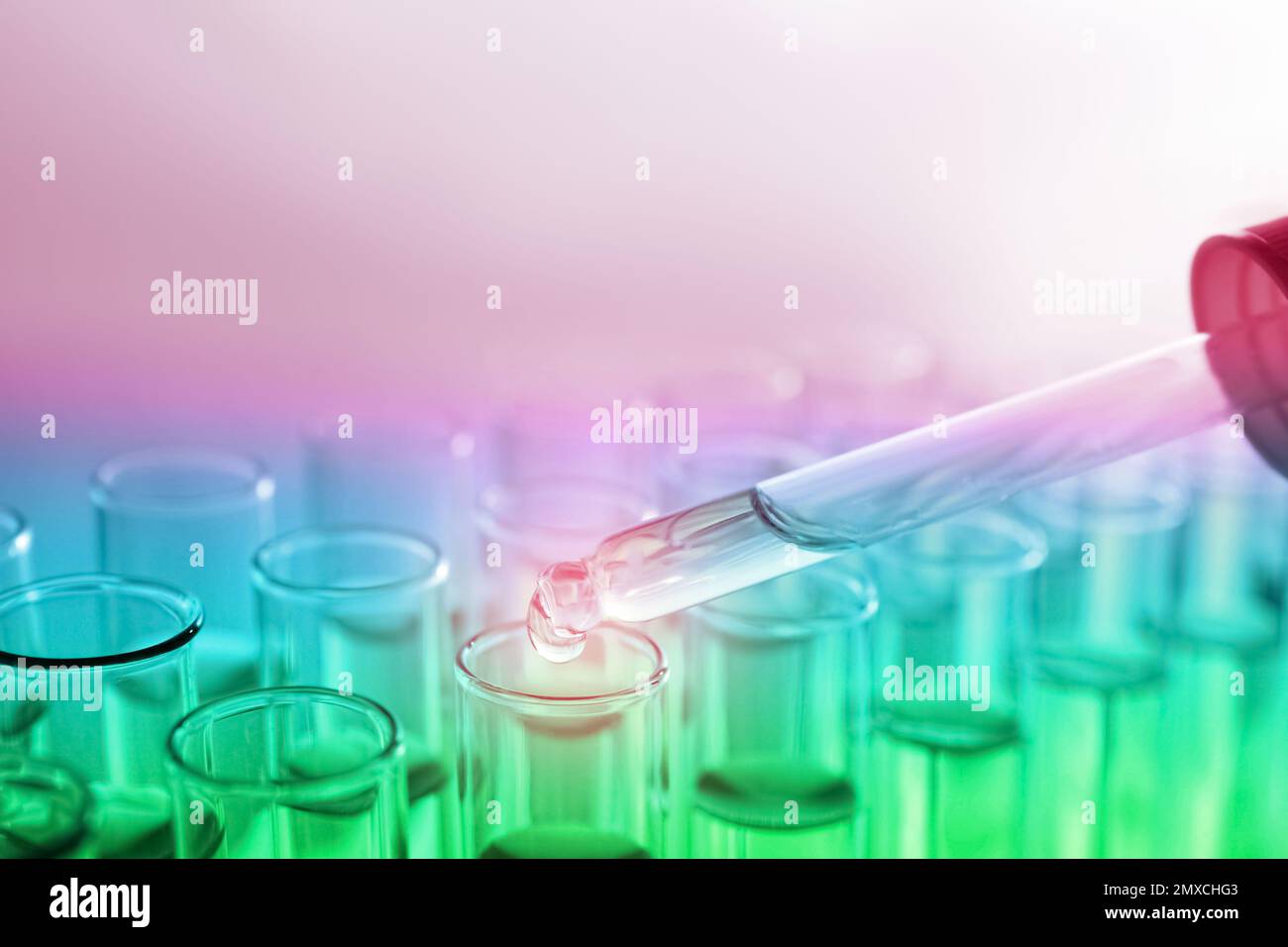 Dropping sample into test tube with liquid on color background, closeup ...