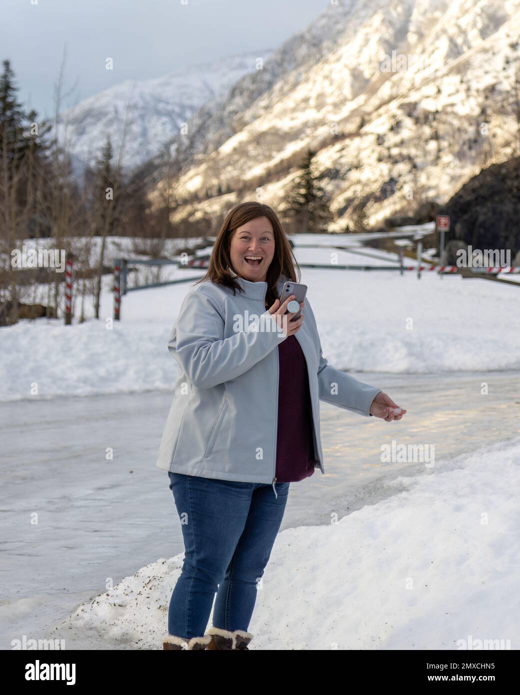 A Caucasian woman holding cell phone and snow standing on icy road in ...