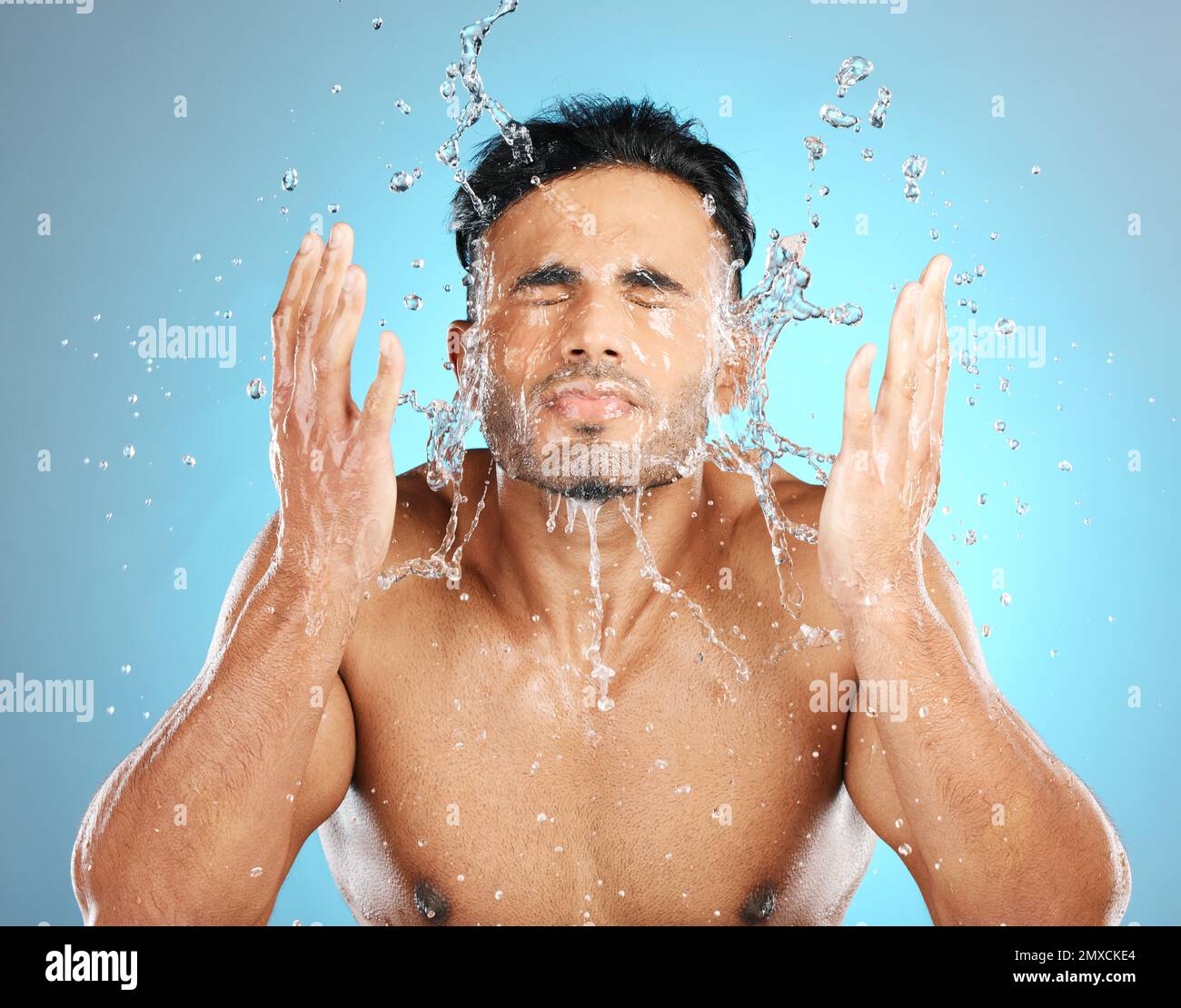 Facial, water splash and man in studio for skincare, wellness or grooming on blue background ...