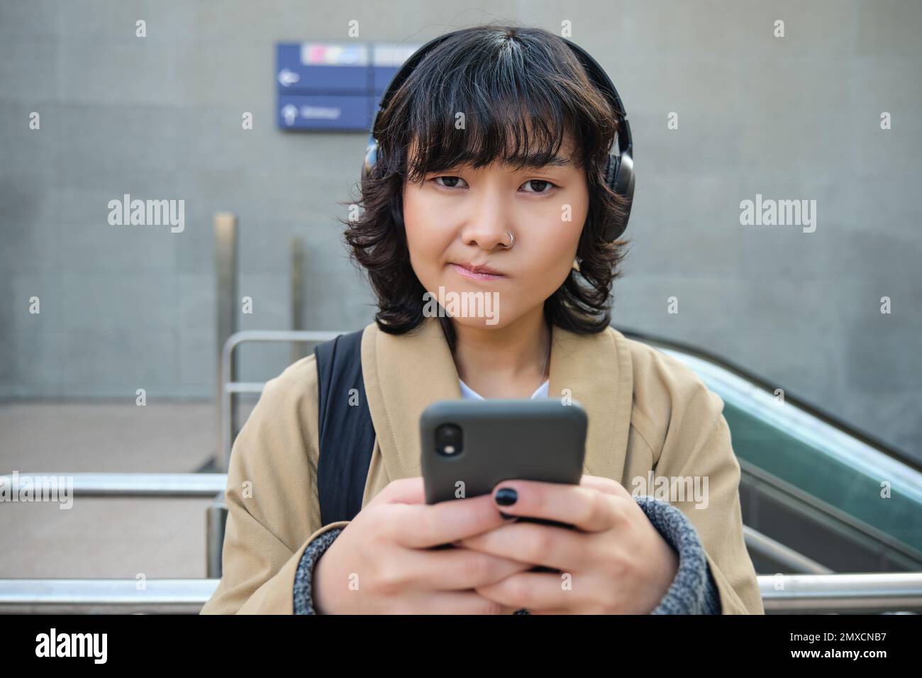 Close up portrait of puzzled, complicated korean girl in headphones, frowns and looks unsure ...