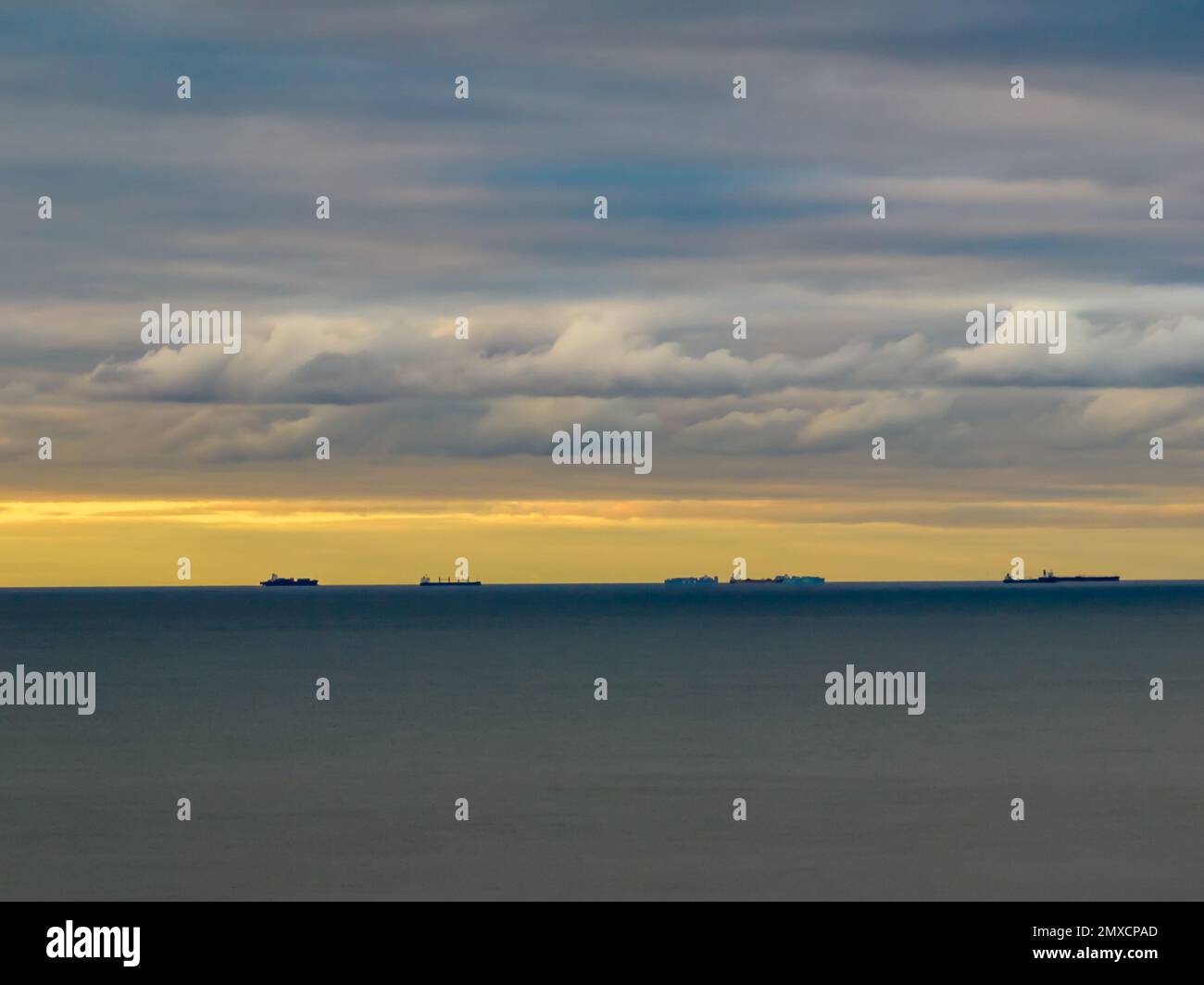 Silhouetted large cargo ships anchored out on the horizon in the ...