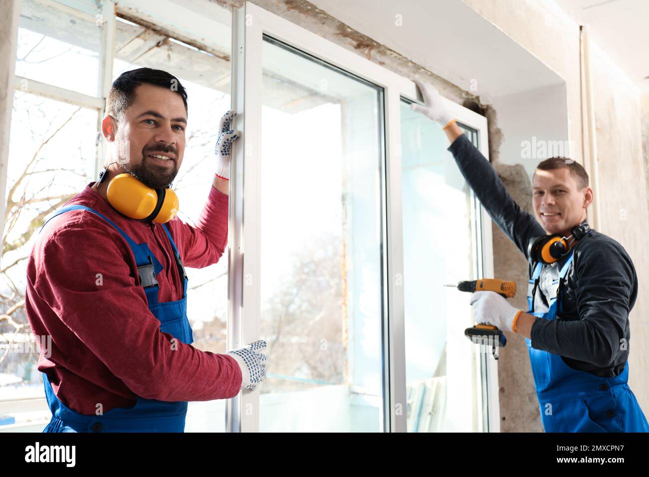 Workers using electric screwdriver for window installation indoors ...