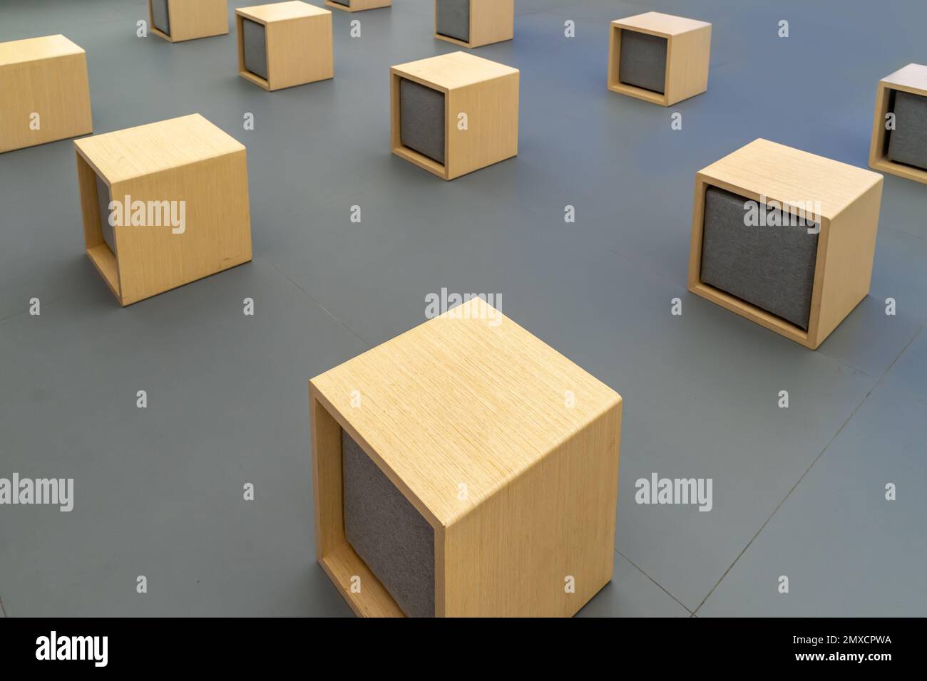 Small wooden square inline chairs on a grey floor Stock Photo - Alamy