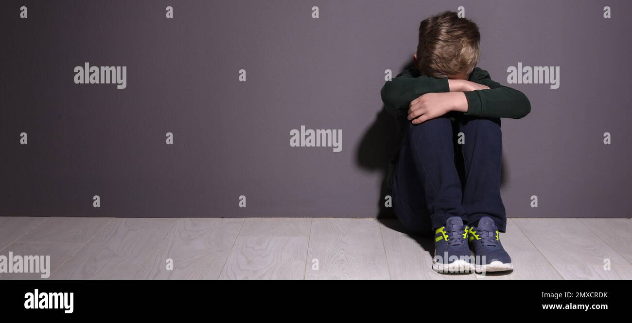 Depressed little boy sitting on floor indoors, banner design with space ...