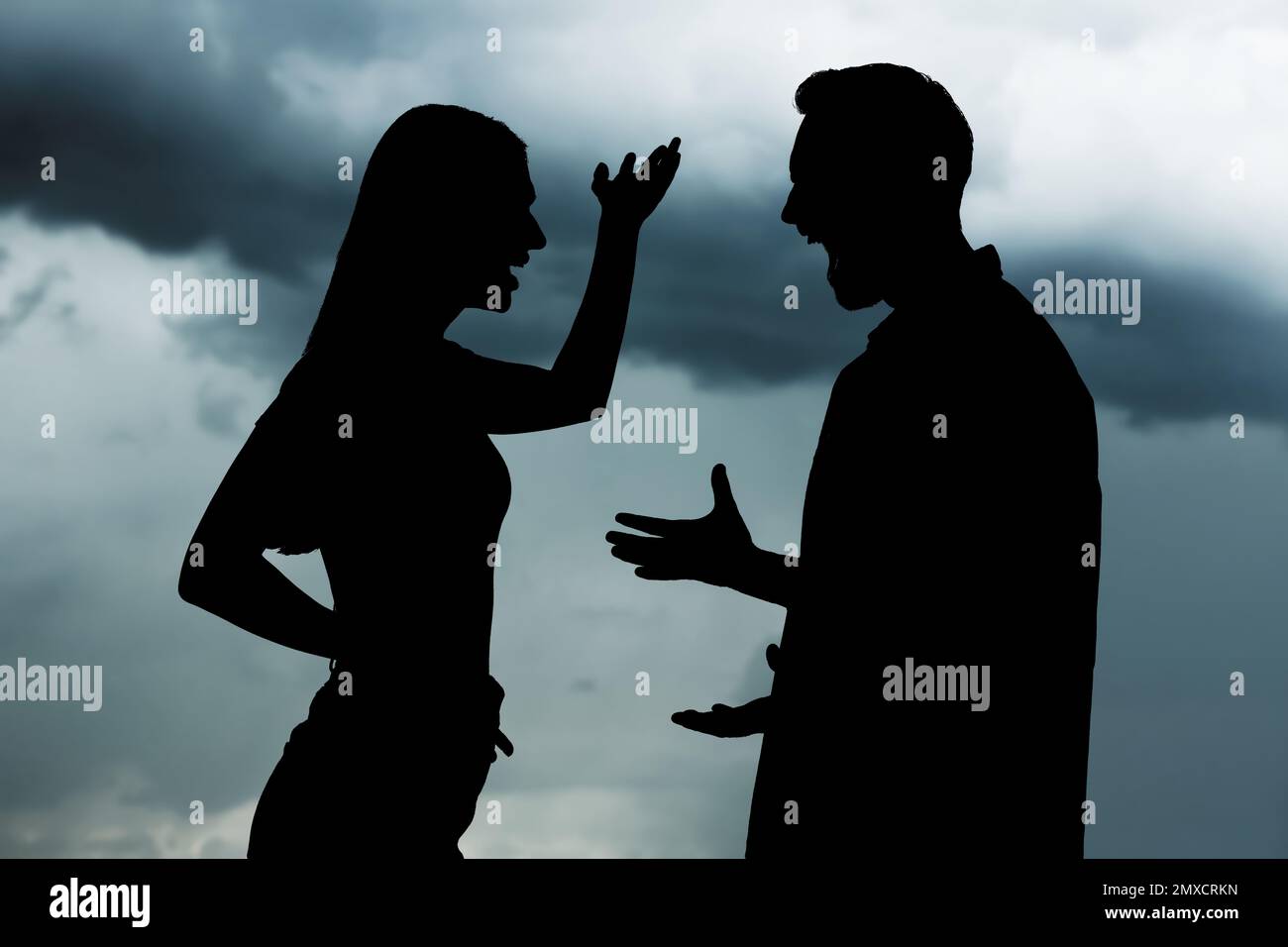 Silhouettes of arguing couple against sky with heavy rainy clouds ...
