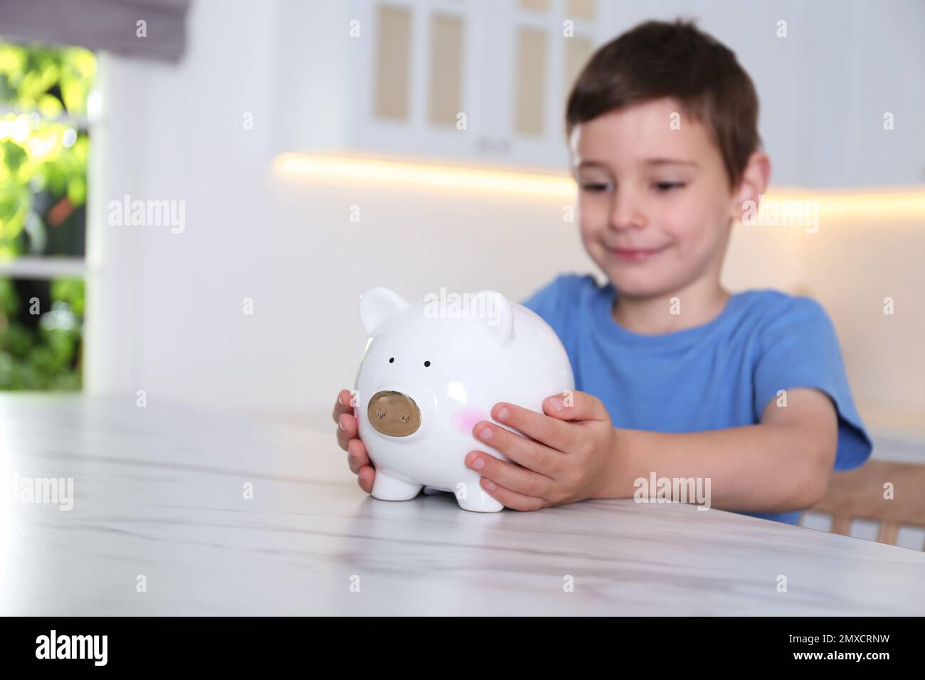 Little boy with piggy bank at marble table indoors Stock Photo - Alamy