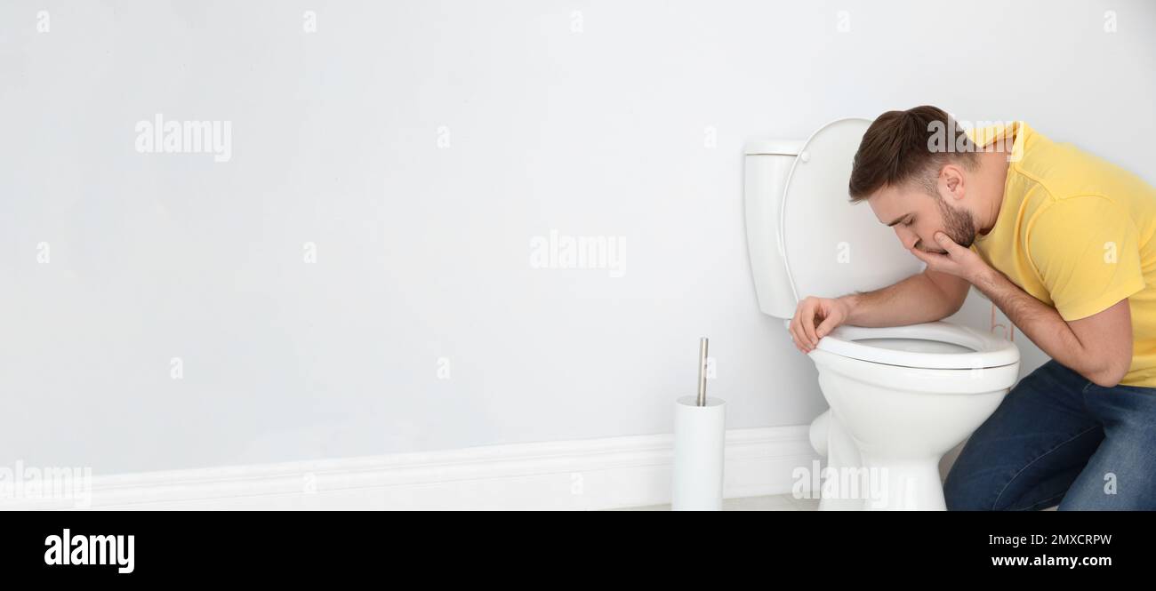 Young man suffering from nausea over toilet bowl indoors, space for ...