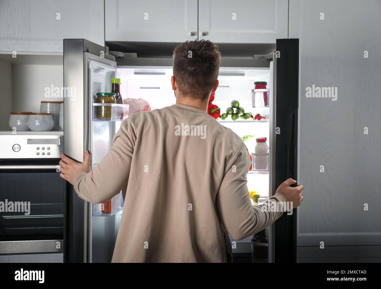 Young man opening refrigerator indoors, back view Stock Photo - Alamy