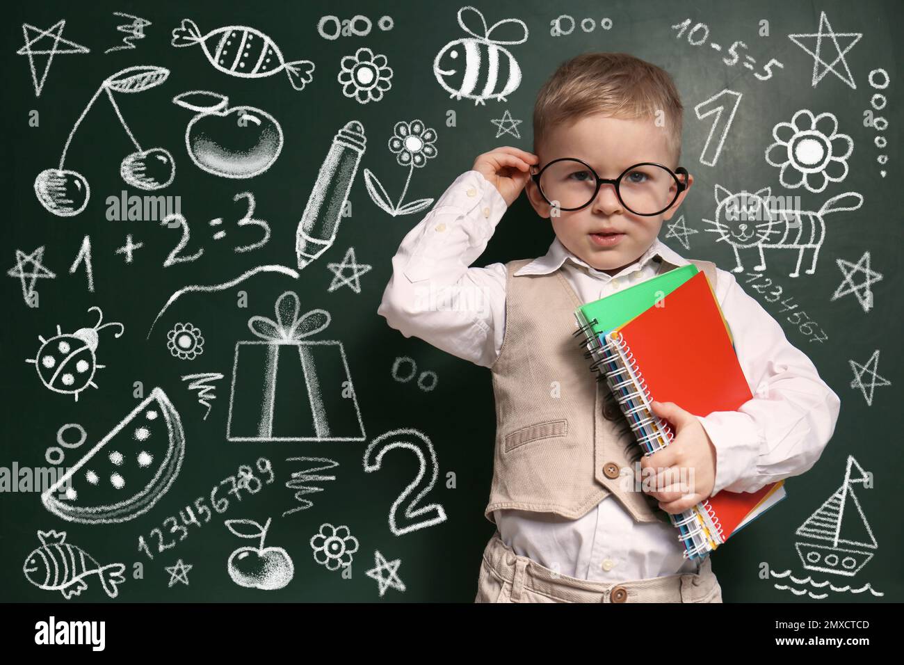 Cute little child in glasses near chalkboard with different drawings ...