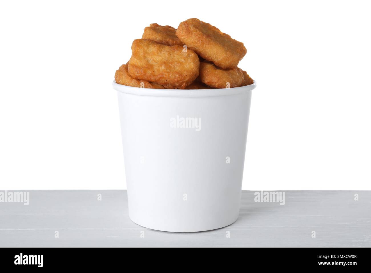 Bucket with tasty chicken nuggets on wooden table against white ...