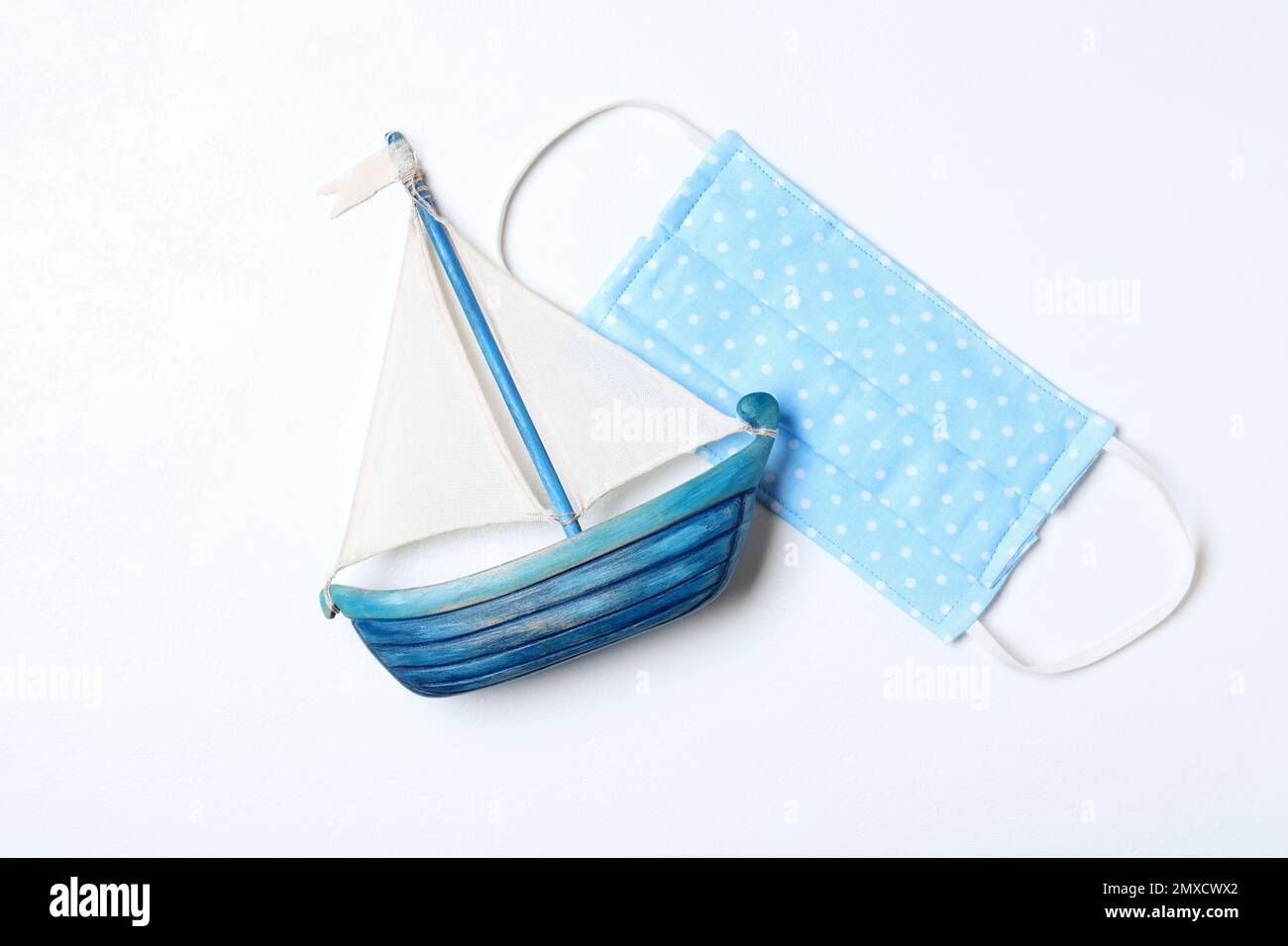 Homemade protective mask and toy sailboat on white background, flat lay ...