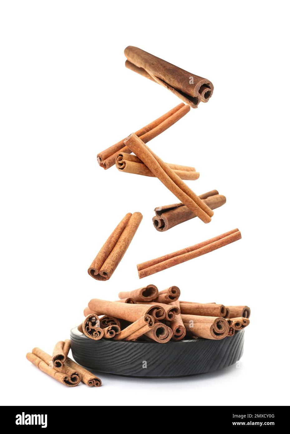 Set with aromatic cinnamon sticks falling into wooden bowl on white ...