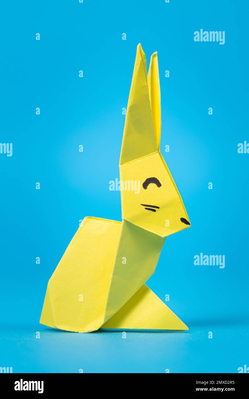 A yellow origami rabbit on a blue background. Crafts for Easter, fold ...