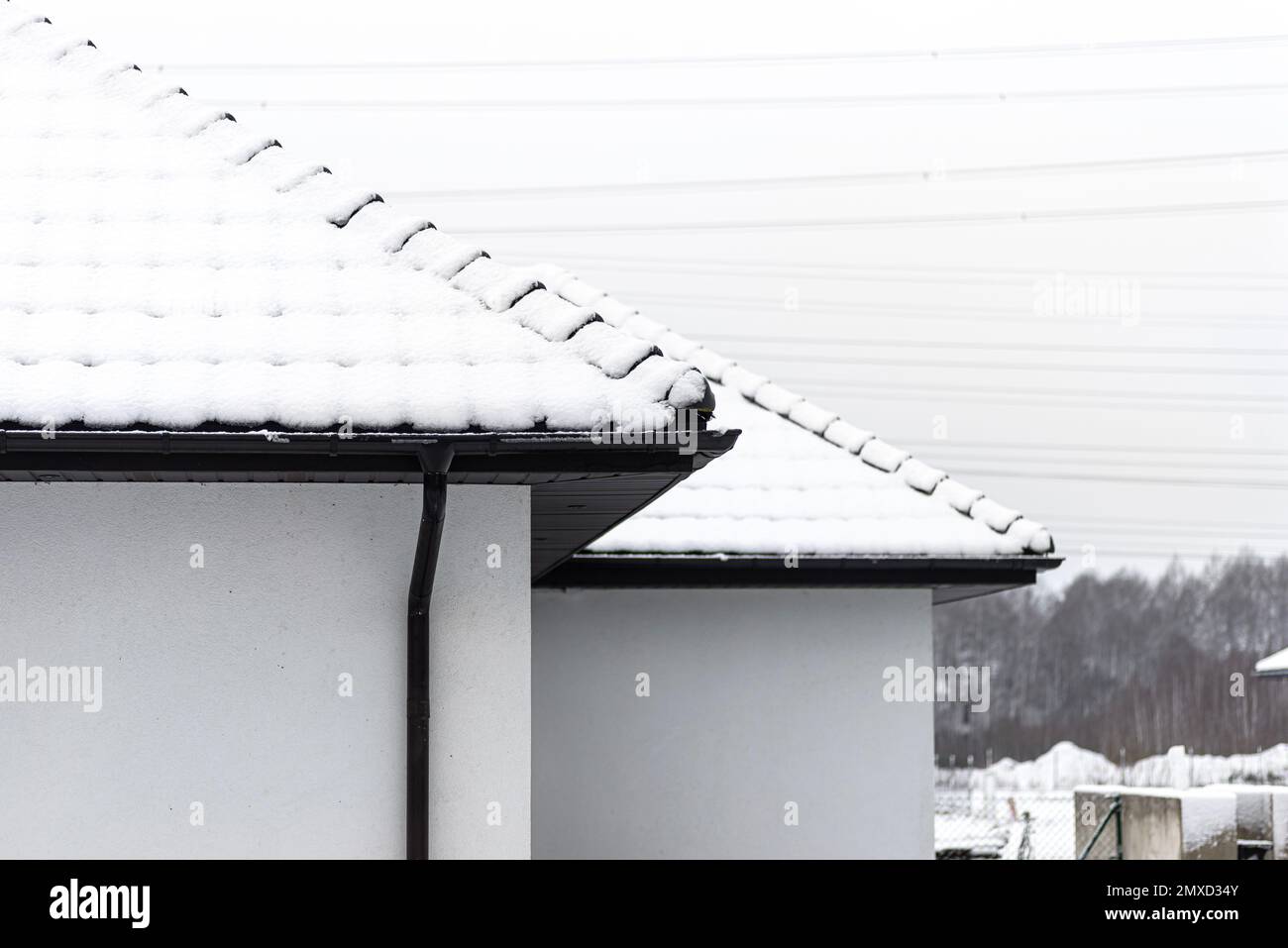 The roof of a single-family house is covered with snow against a cloudy ...