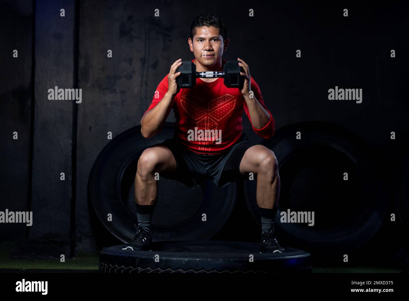 A young Mexican latino male working out and weightlifting in a dark gym ...