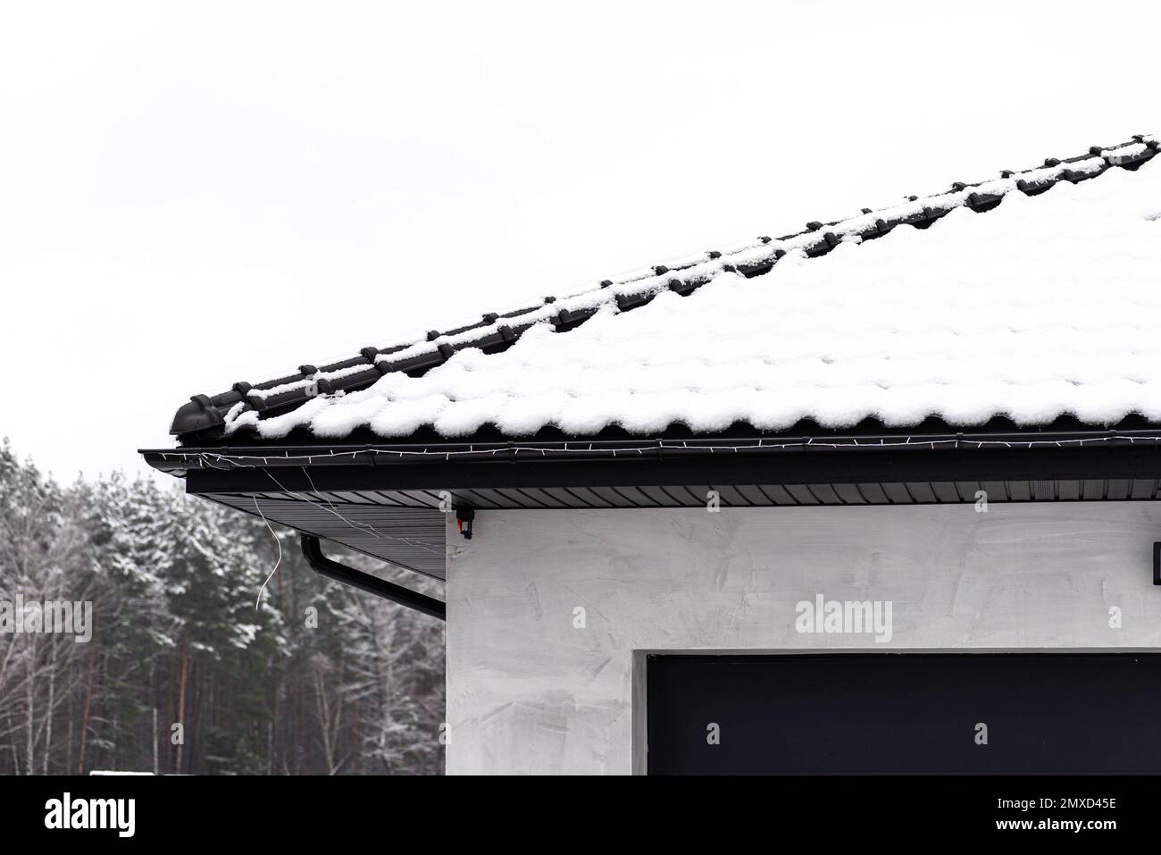The roof of a single-family house is covered with snow against a cloudy ...