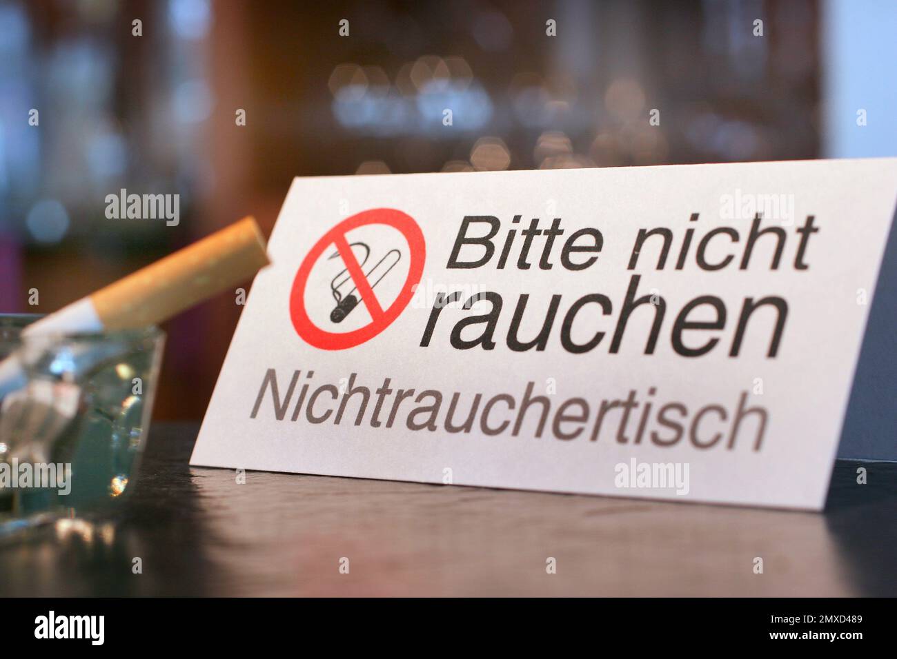 cigarette in an ashtray in front of a sign 'Bitte nicht rauchen ...