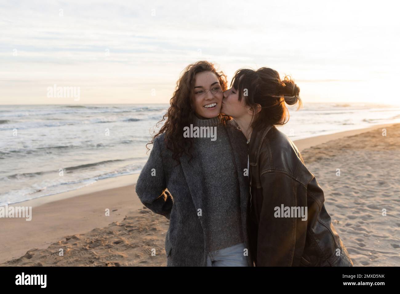 Young woman kissing cheek of smiling friend on beach in Barcelona Stock ...
