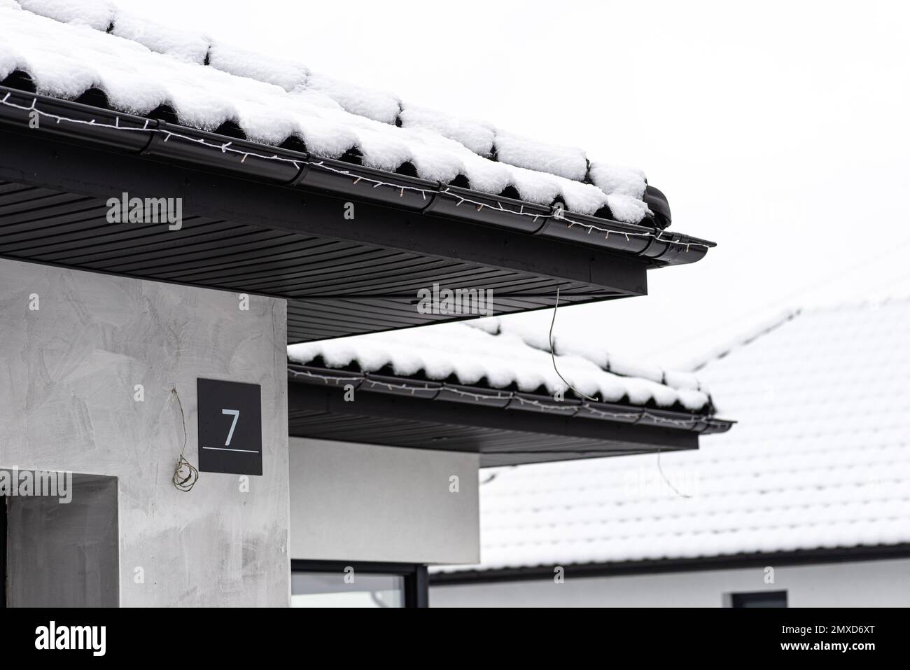 The roof of a single-family house is covered with snow against a cloudy ...