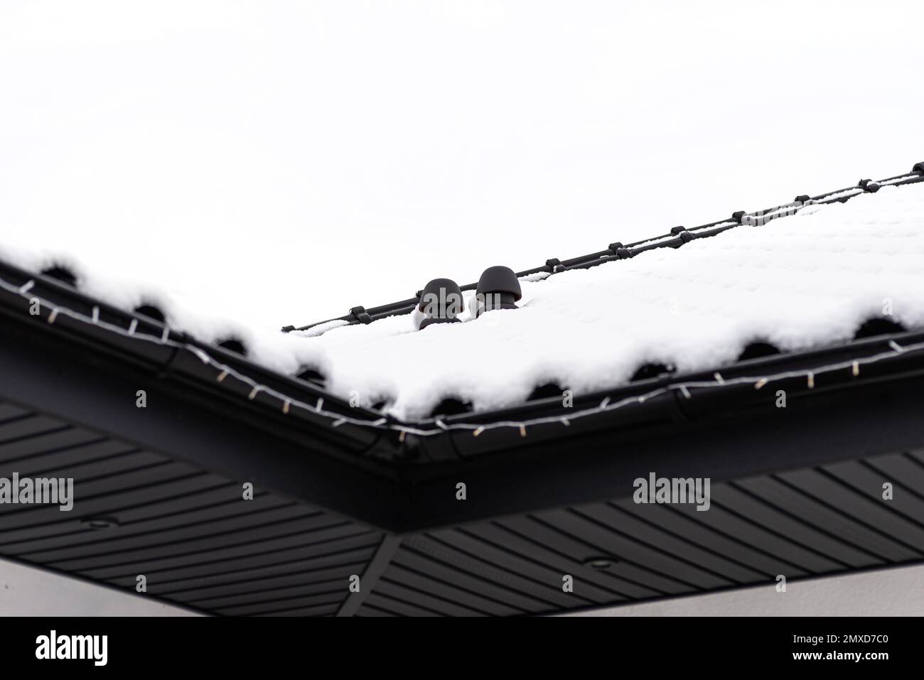 The roof of a single-family house is covered with snow against a cloudy ...