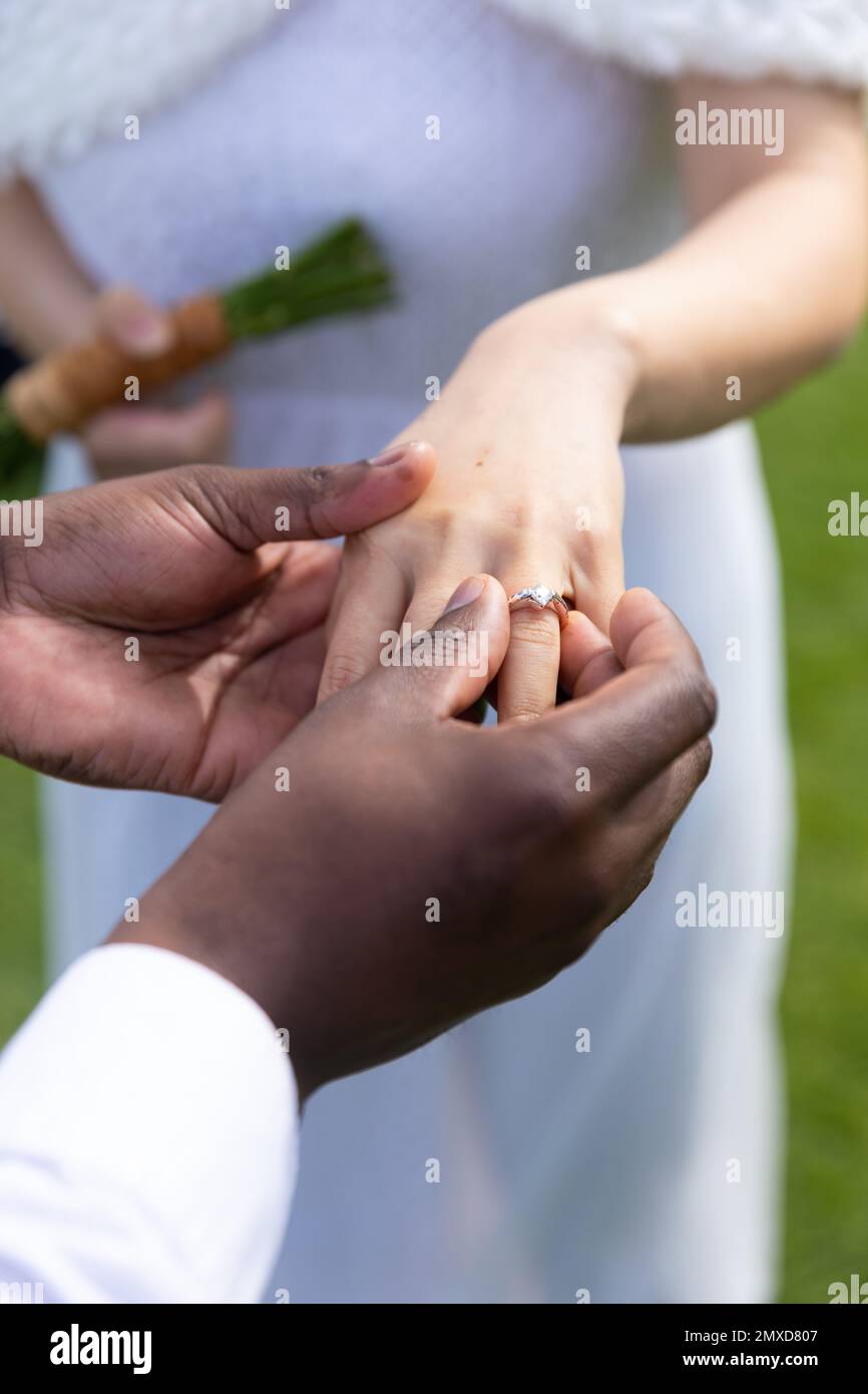 Vertical midsection of diverse groom placing ring on finger of bride at ...
