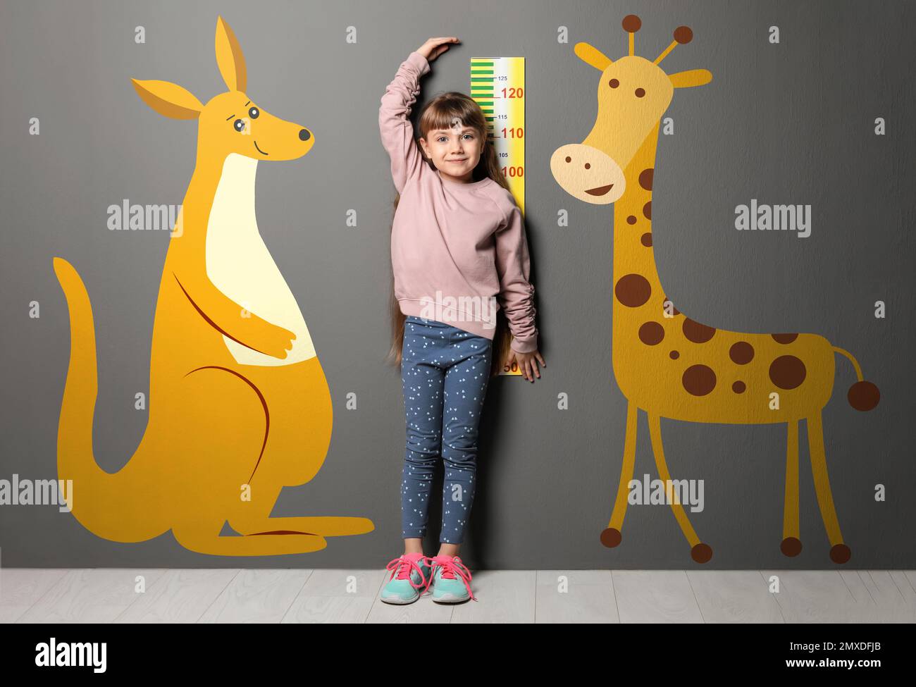 Little girl measuring height and drawings of animals near grey wall ...