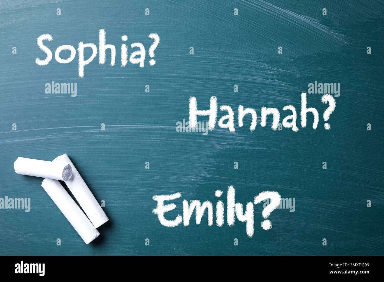 Pieces of white chalk and different baby names written on greenboard ...