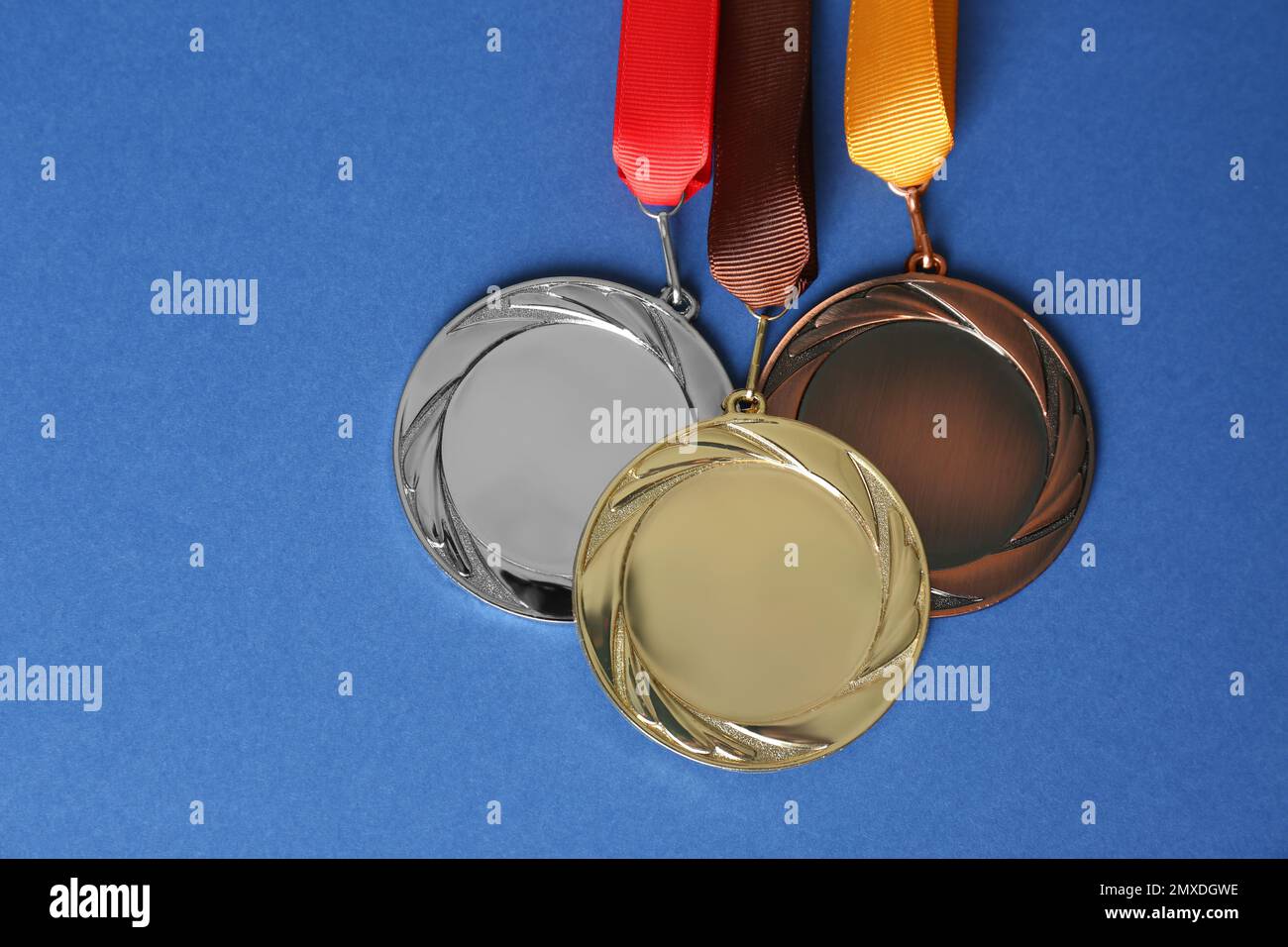 Gold, silver and bronze medals on blue background, flat lay. Space for ...