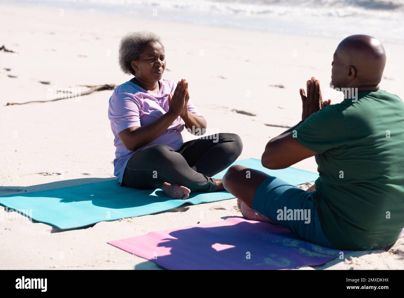 African american senior couple meditating in prayer pose on yoga mats at beach during summer ...