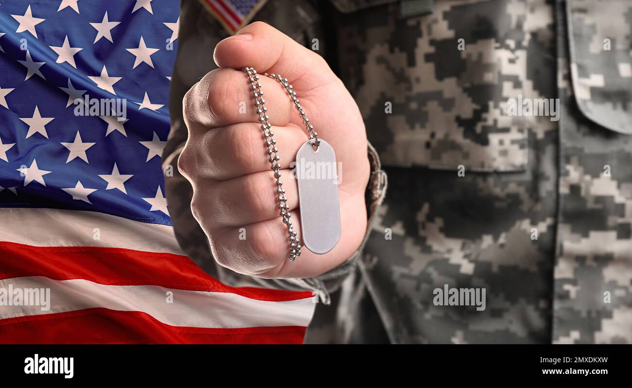 Male soldier holding military ID tag and American flag on background ...