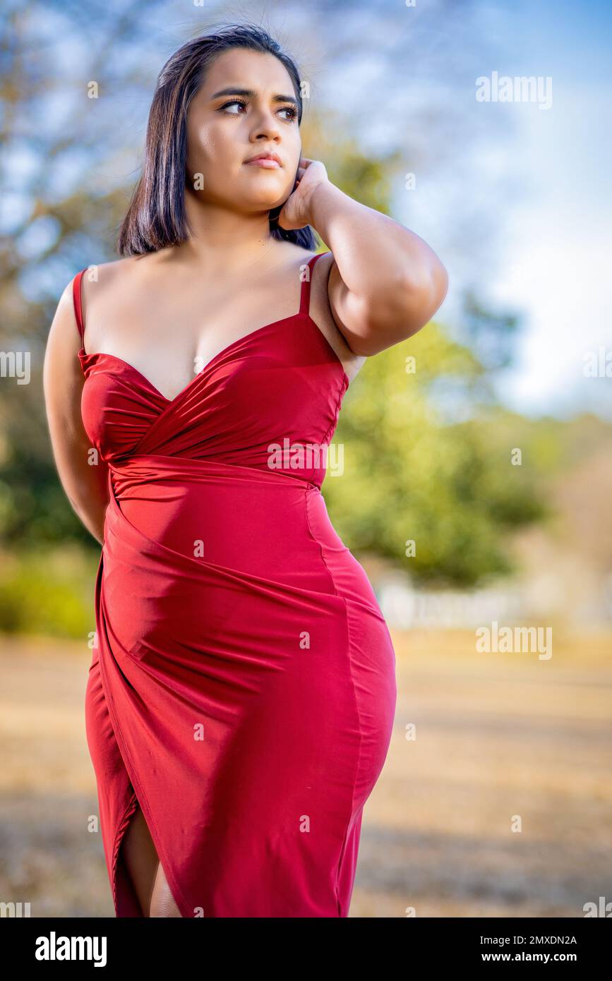 A beautiful Hispanic model posing in a red dress outdoors during ...