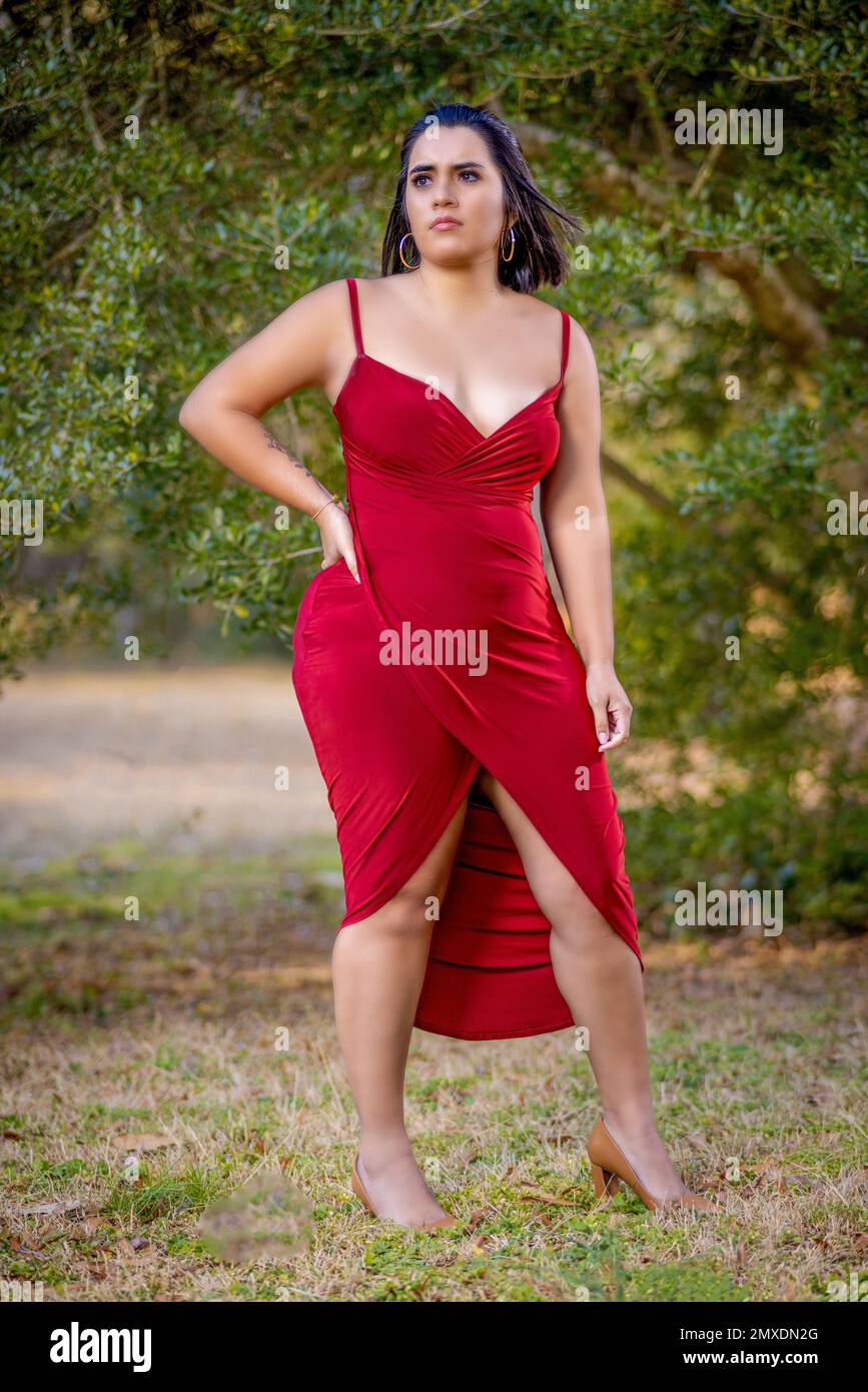 A beautiful Hispanic model posing in a red dress outdoors during ...