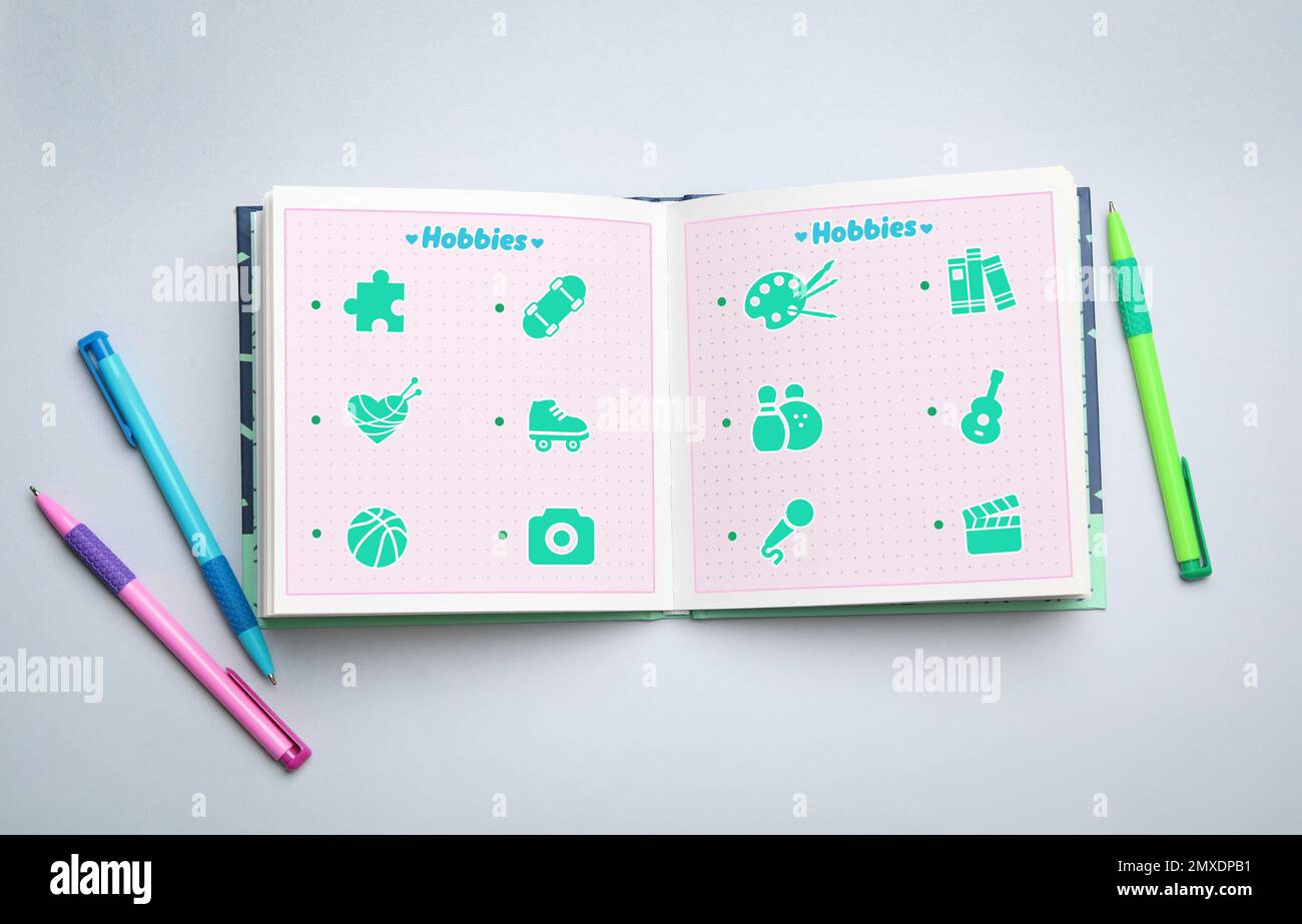 Open notebook with icons of different hobbies and pens on light ...