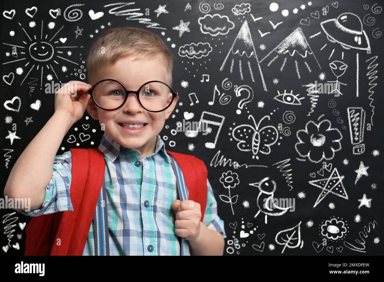Cute little child in glasses near chalkboard with different drawings ...