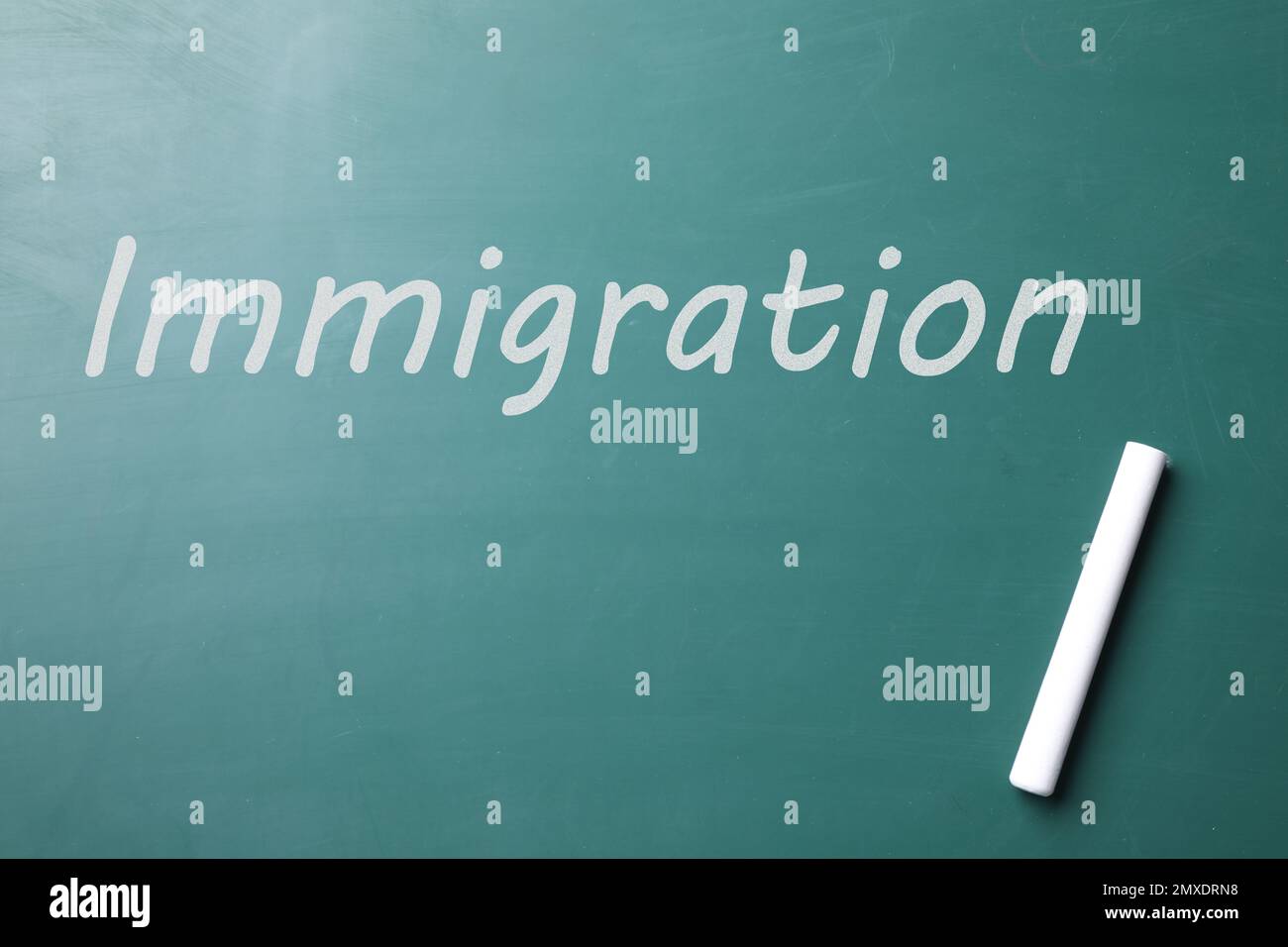 Piece of white chalk and word IMMIGRATION written on greenboard, top ...