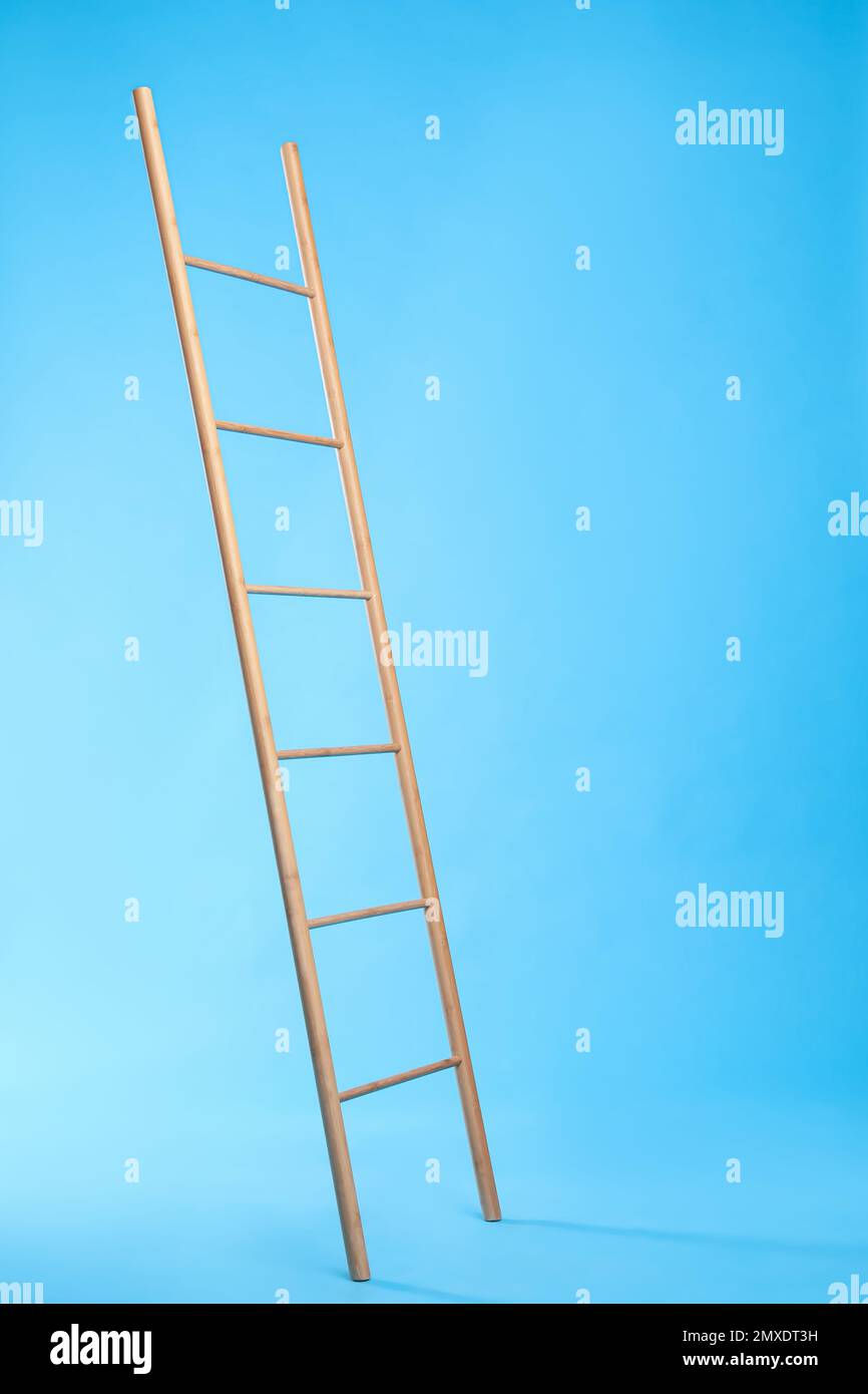 Modern wooden ladder on light blue background Stock Photo - Alamy