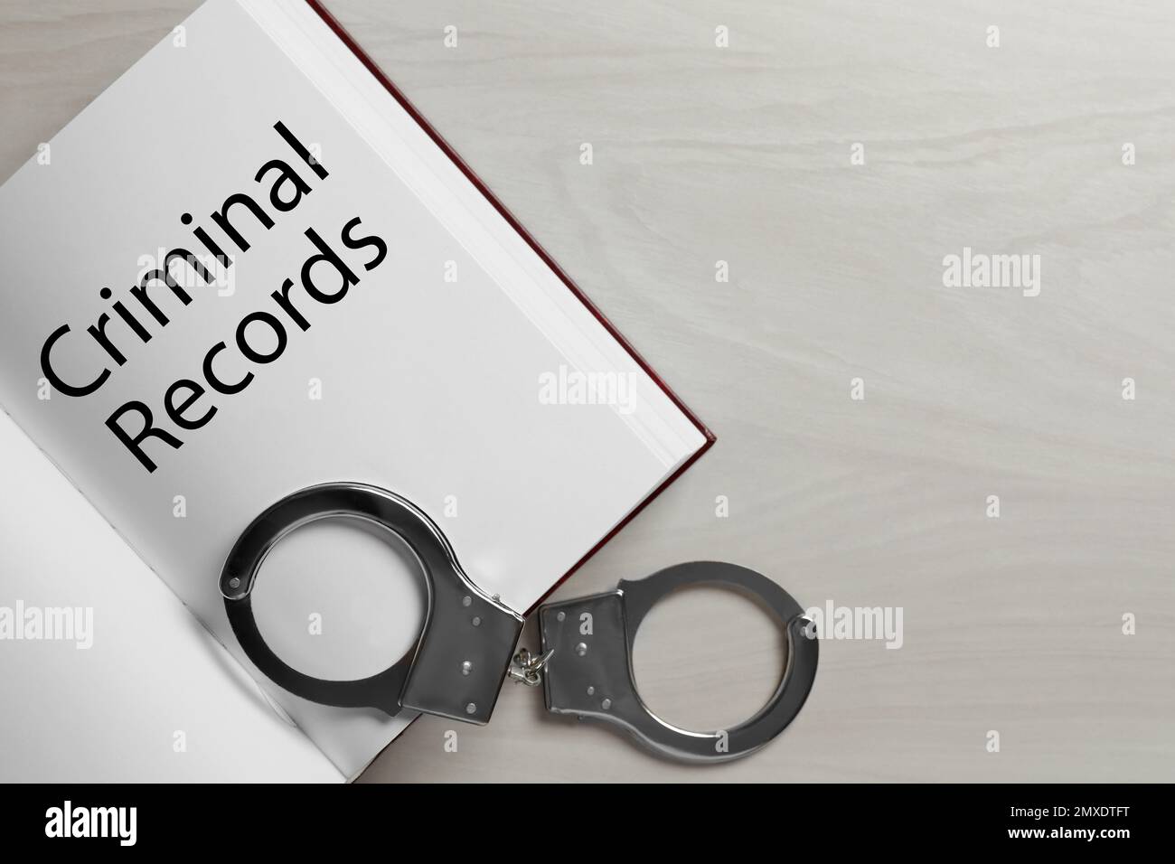 Book with words CRIMINAL RECORDS and handcuffs on white wooden ...