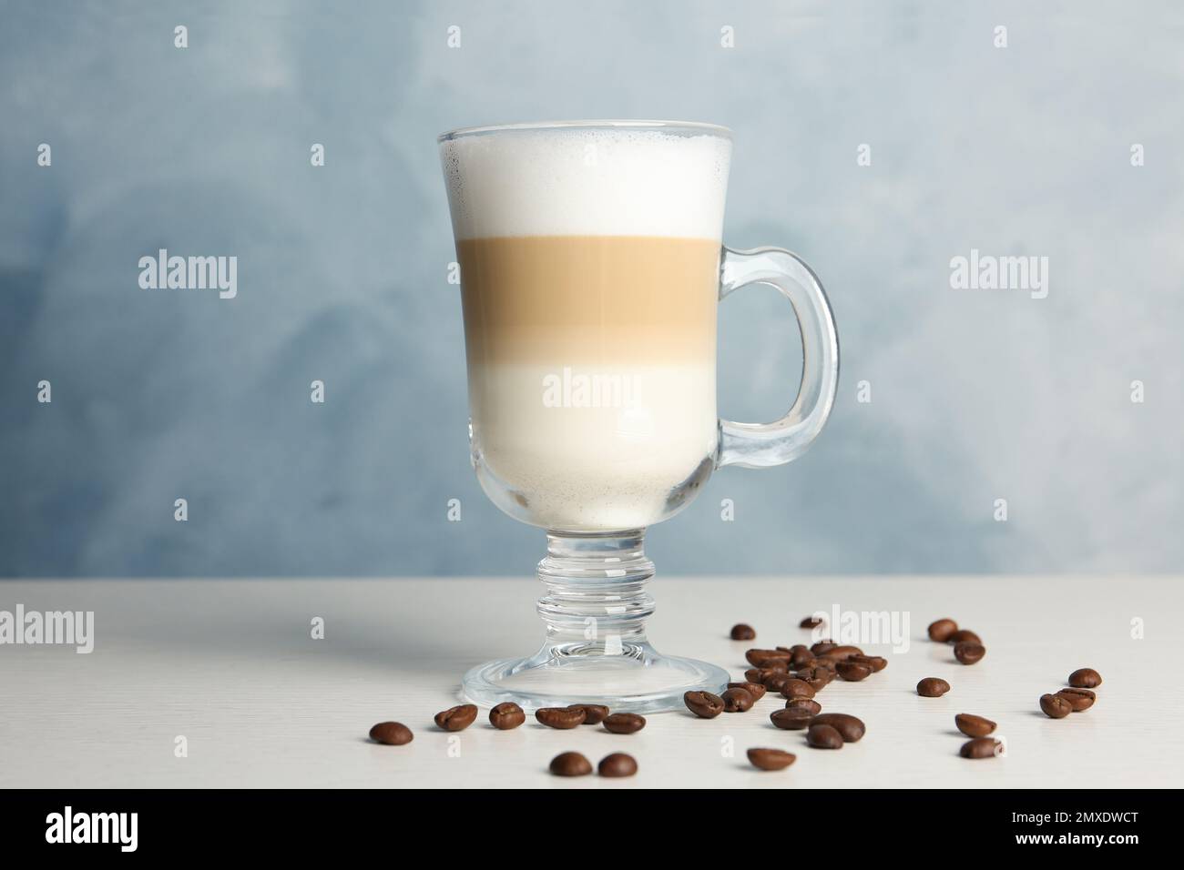 Delicious latte macchiato and coffee beans on white table against light ...