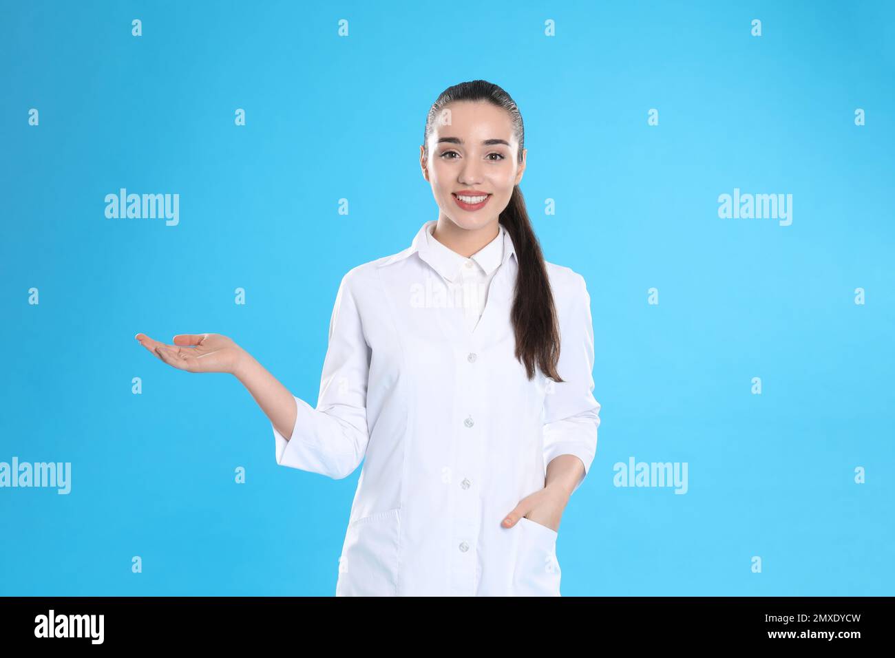 Happy young woman in lab coat on light blue background Stock Photo - Alamy
