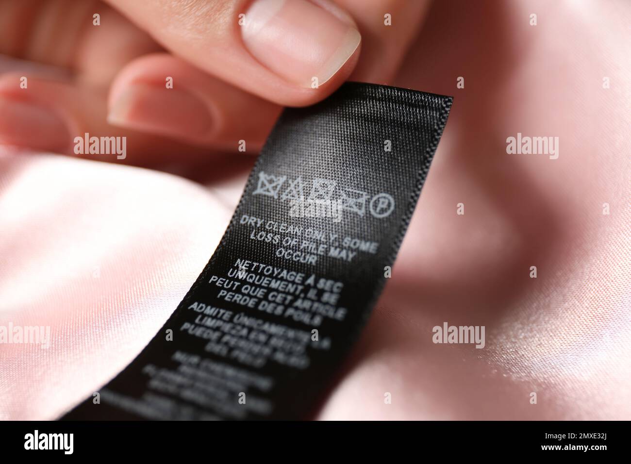 Woman reading clothing label with care symbols on pink silk shirt ...