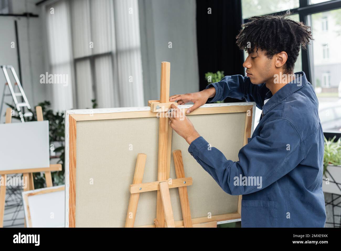 Side view of young african american artist adjusting easel with canvas ...