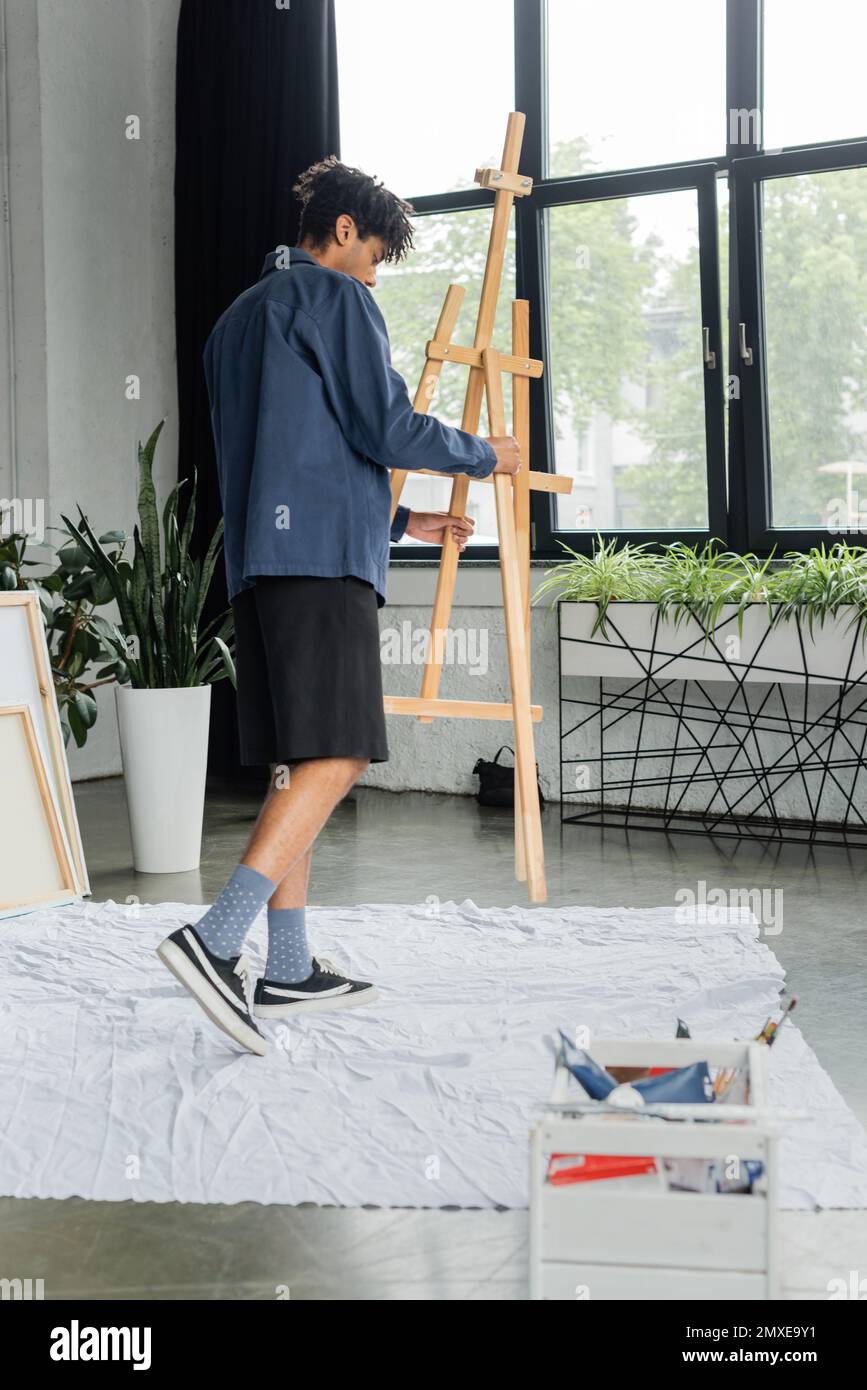 Side view of african american artist holding easel in studio,stock ...