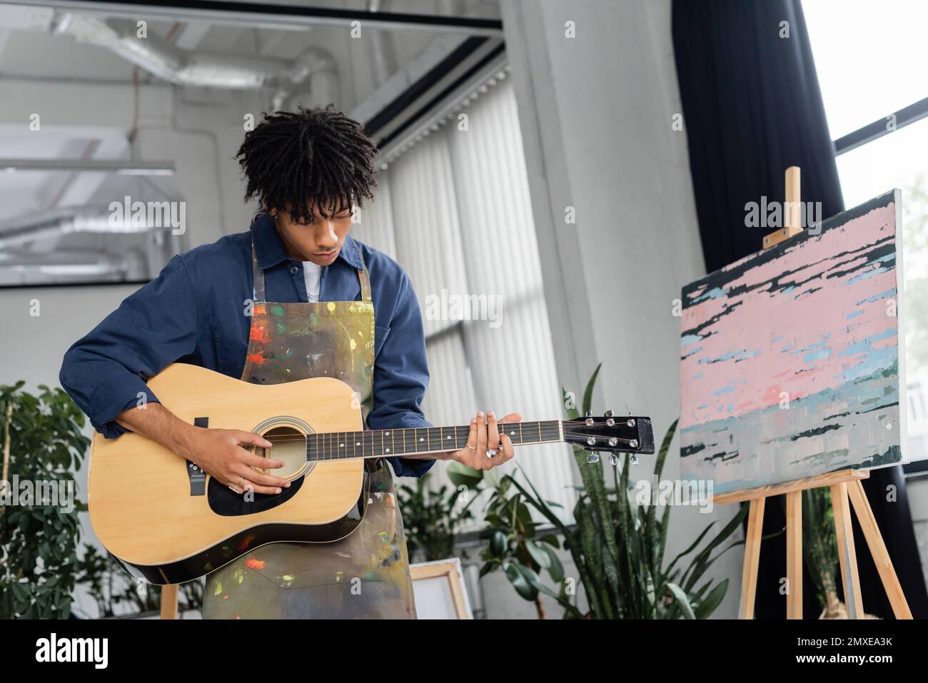Young african american artist in apron playing acoustic guitar in ...