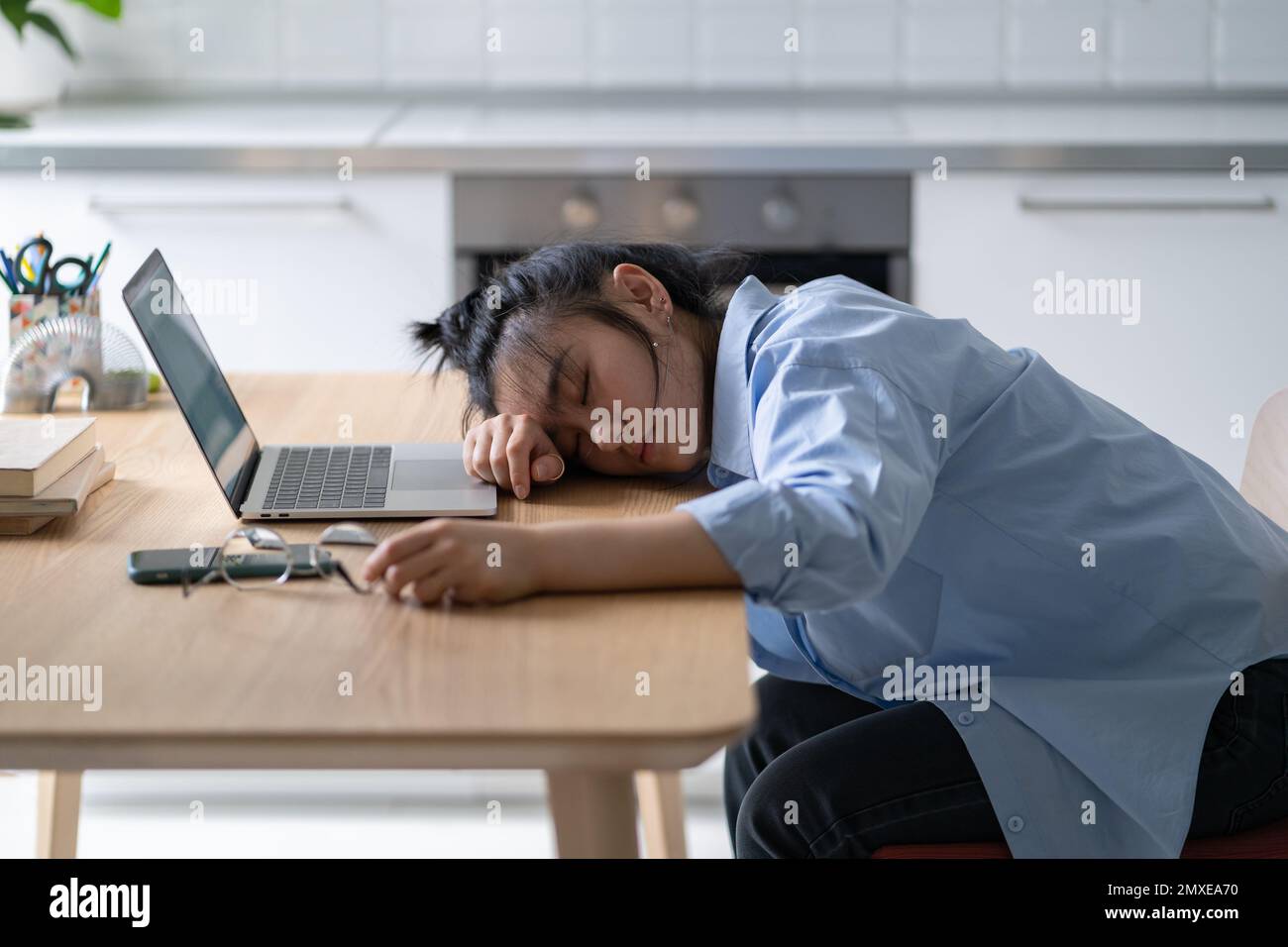 Tired exhausted Asian woman sleeping in kitchen with head on desk near ...