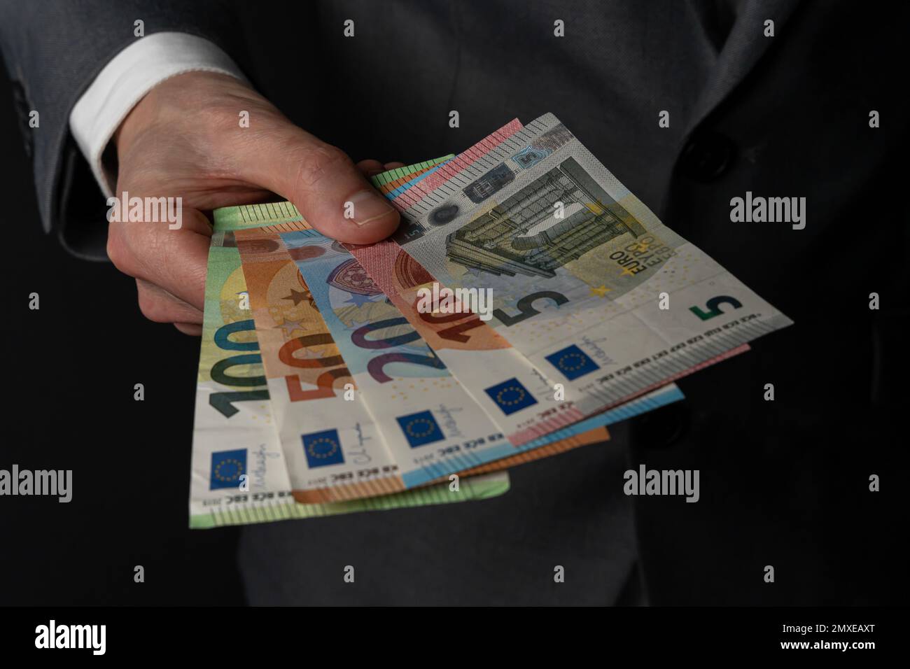 still life. A man in a business suit holds fanned euro banknotes of ...