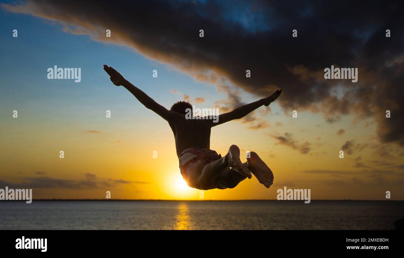 A man jumping into the ocean with the golden sunset and the horizon in ...