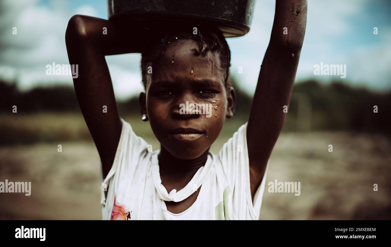 A beautiful black little girl carrying a bowl of water on her head in ...