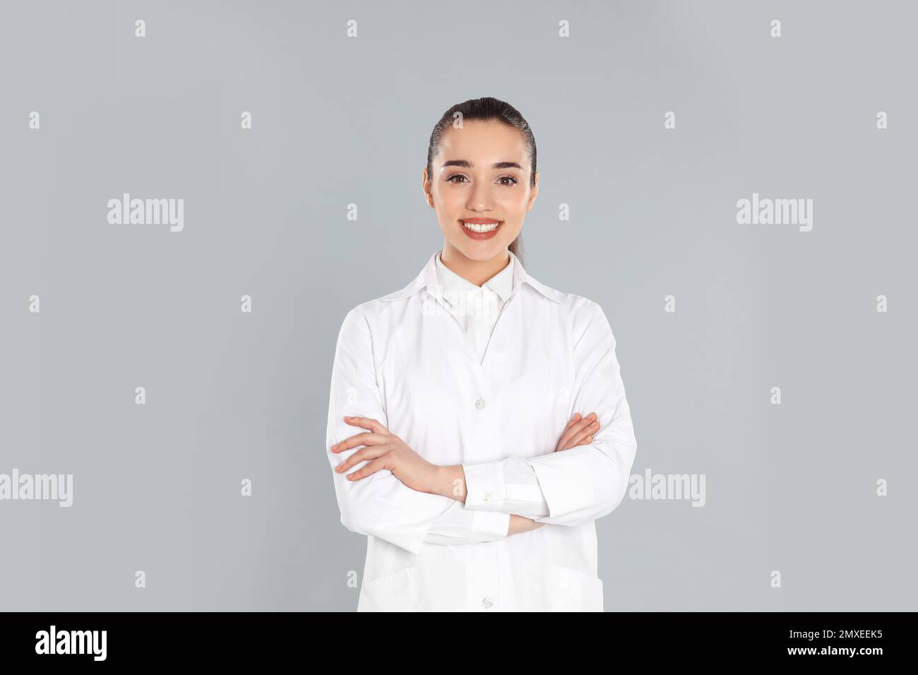 Happy young woman in lab coat on light grey background Stock Photo - Alamy