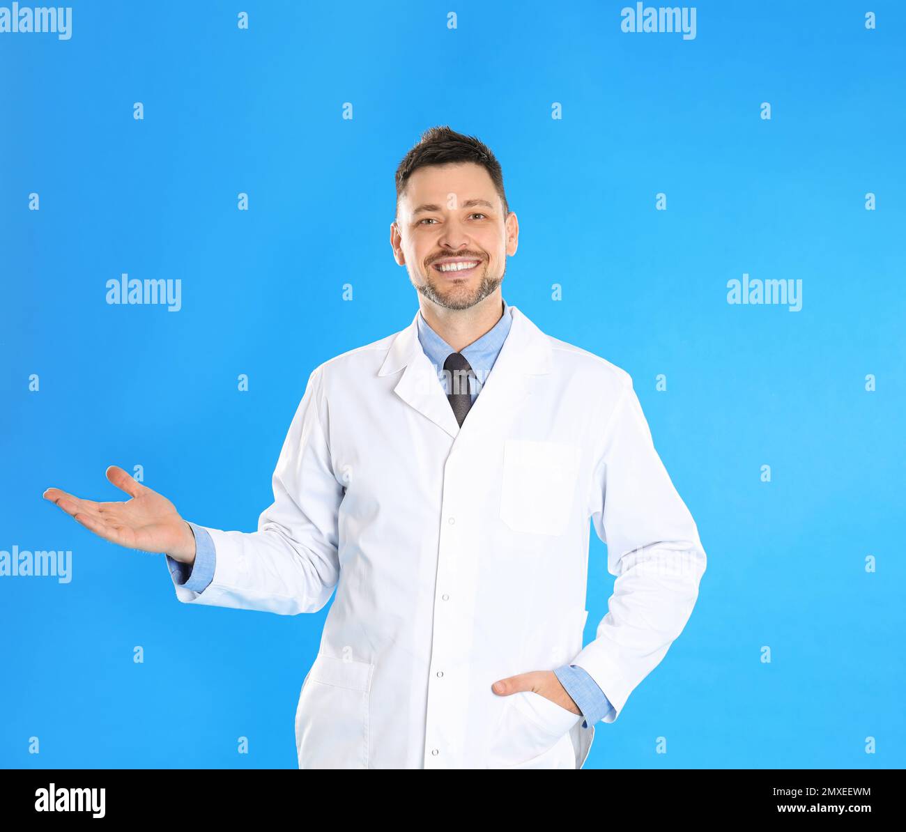 Happy man in lab coat on light blue background Stock Photo - Alamy